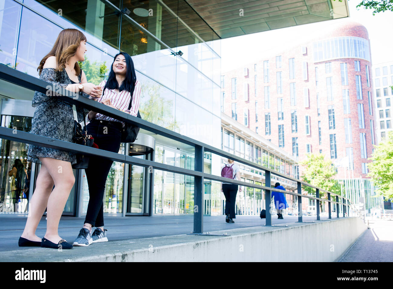 Two young female students stand outside their college modern buildings ...