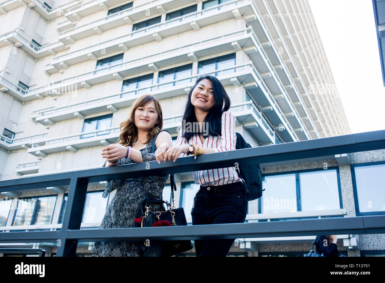 Two young female students stand outside their college modern buildings ...
