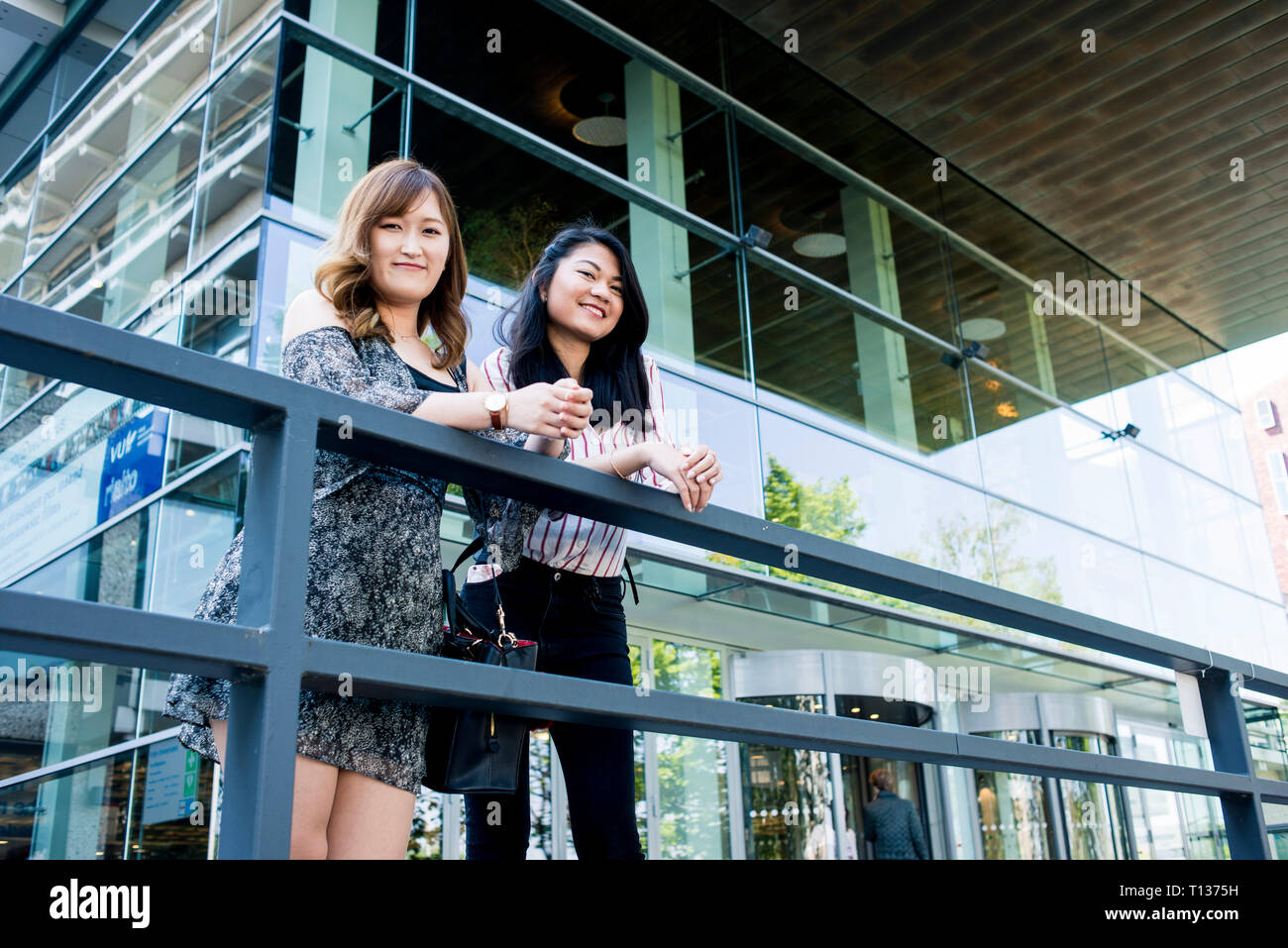 Two young female students stand outside their college modern buildings ...