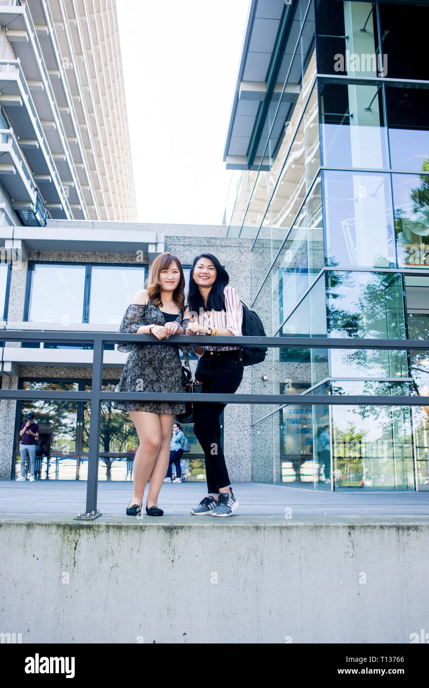 Two young female students stand outside their college modern buildings ...