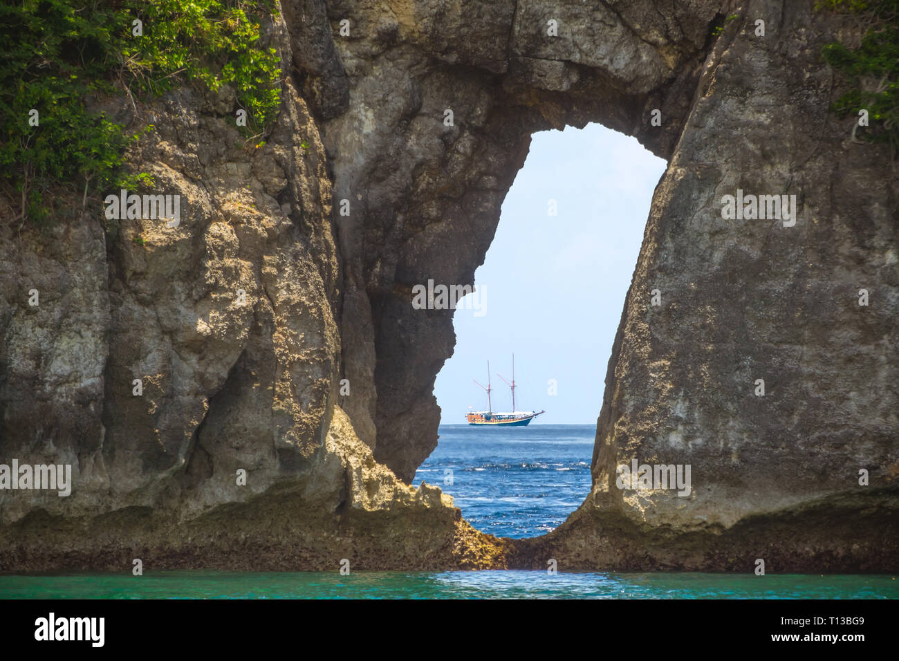 Small rocky island. A sailboat on the horizon is visible through a ...