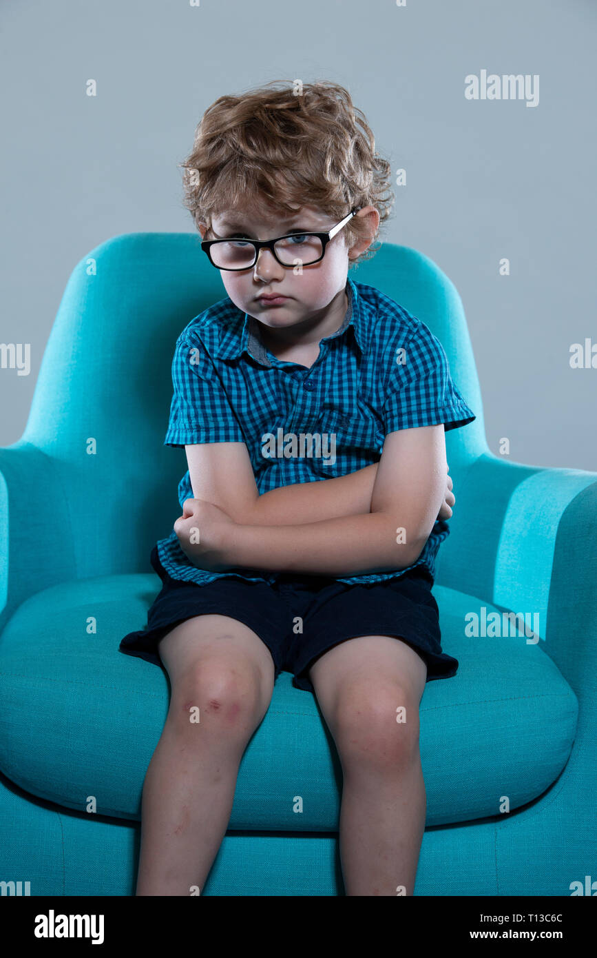 a board young white boy being restless and fed up on a colourful sofa ...