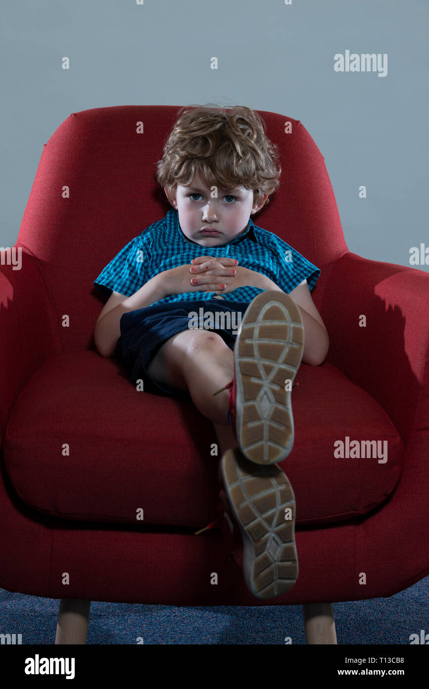 a board young white boy being restless and fed up on a colourful sofa ...