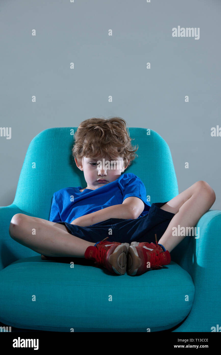 a board young white boy being restless and fed up on a colourful sofa ...