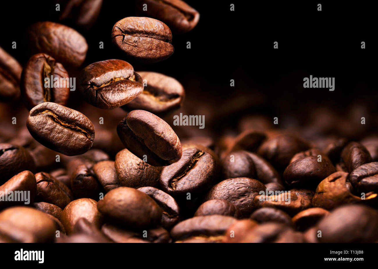 Coffee beans falling on pile, black background with copy space, close ...