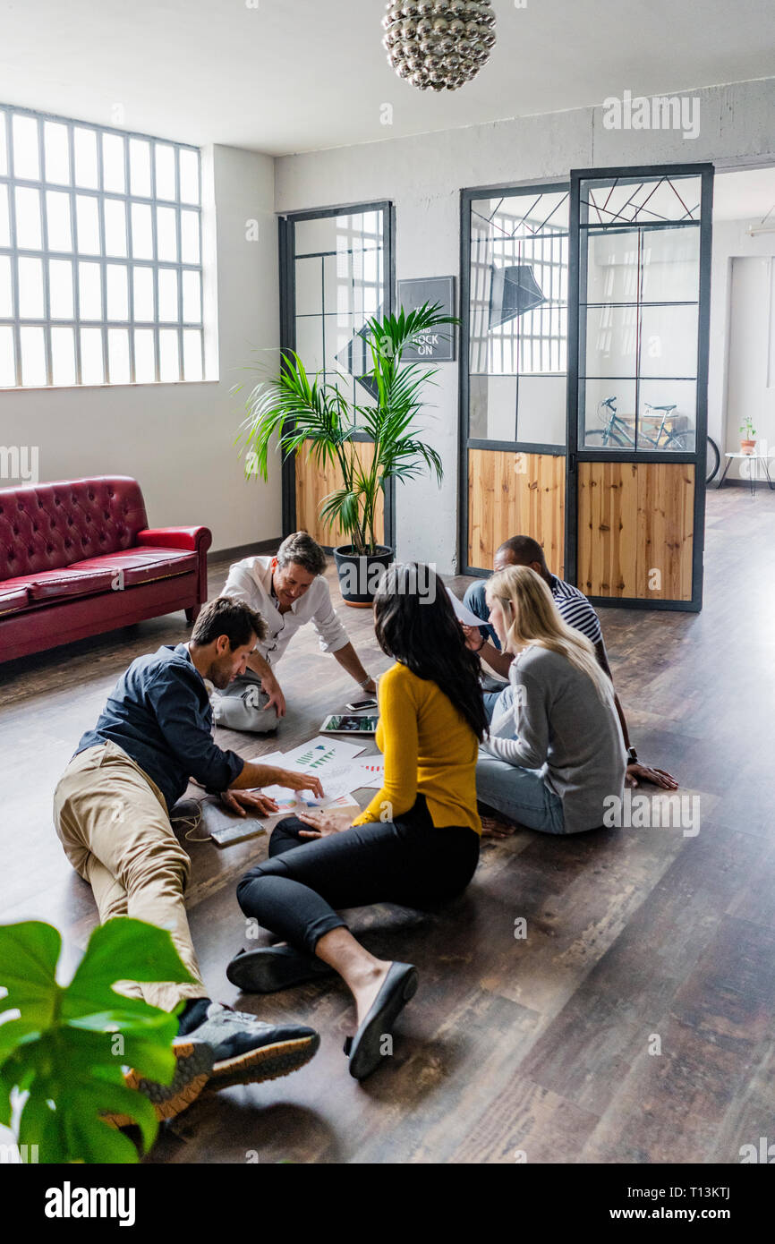 Business team sitting on floor discussing documents in loft office ...