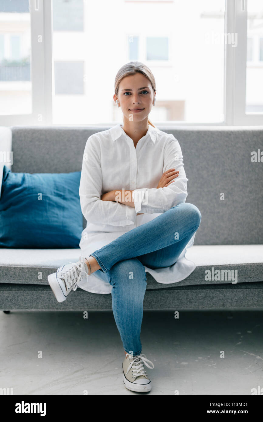 Young woman sitting on couch, with arms crossed Stock Photo - Alamy