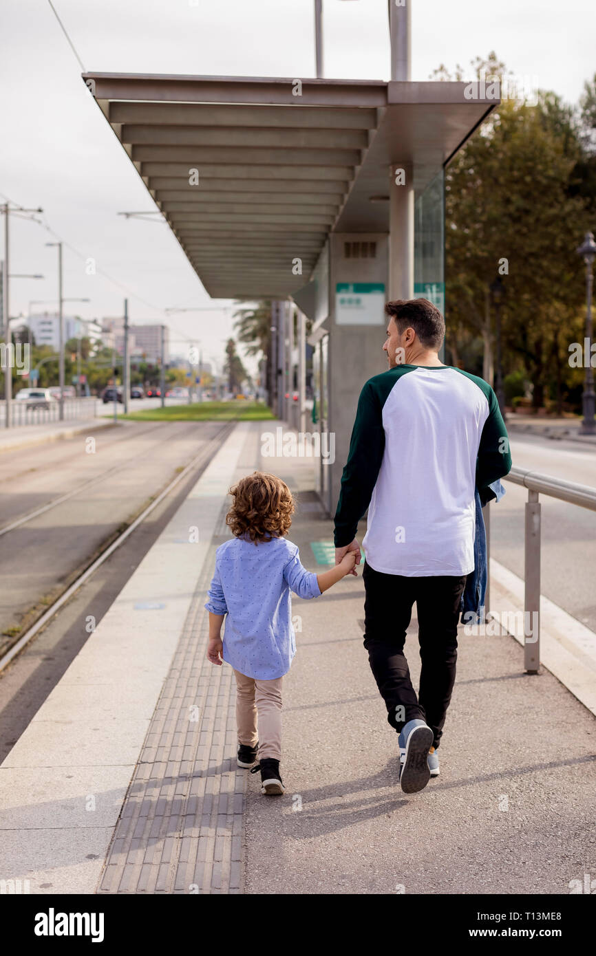 Rear view of father and son walking hand in hand at tram stop in the ...