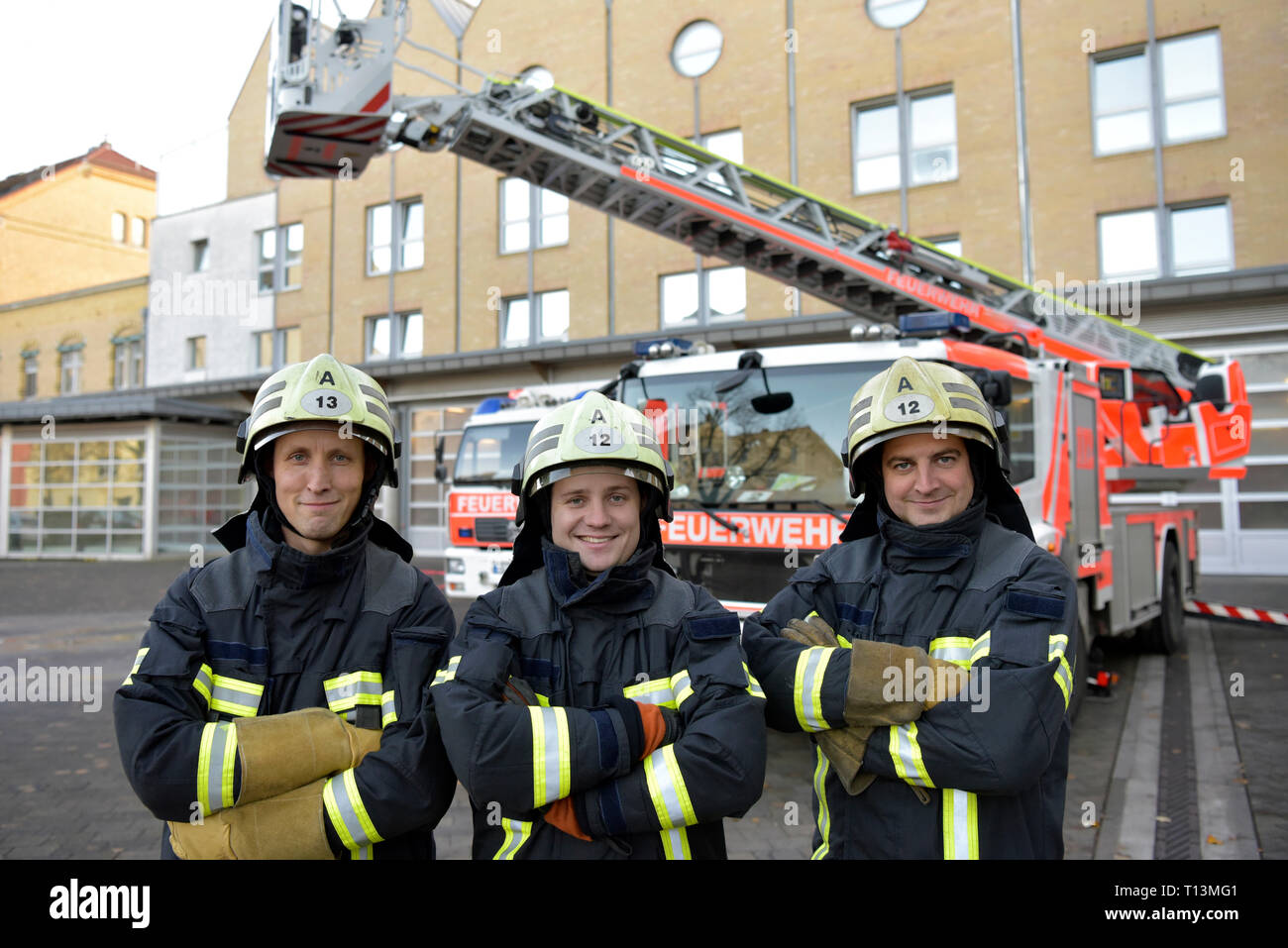 Portrait of three smiling firefighters standing on yard in front of ...