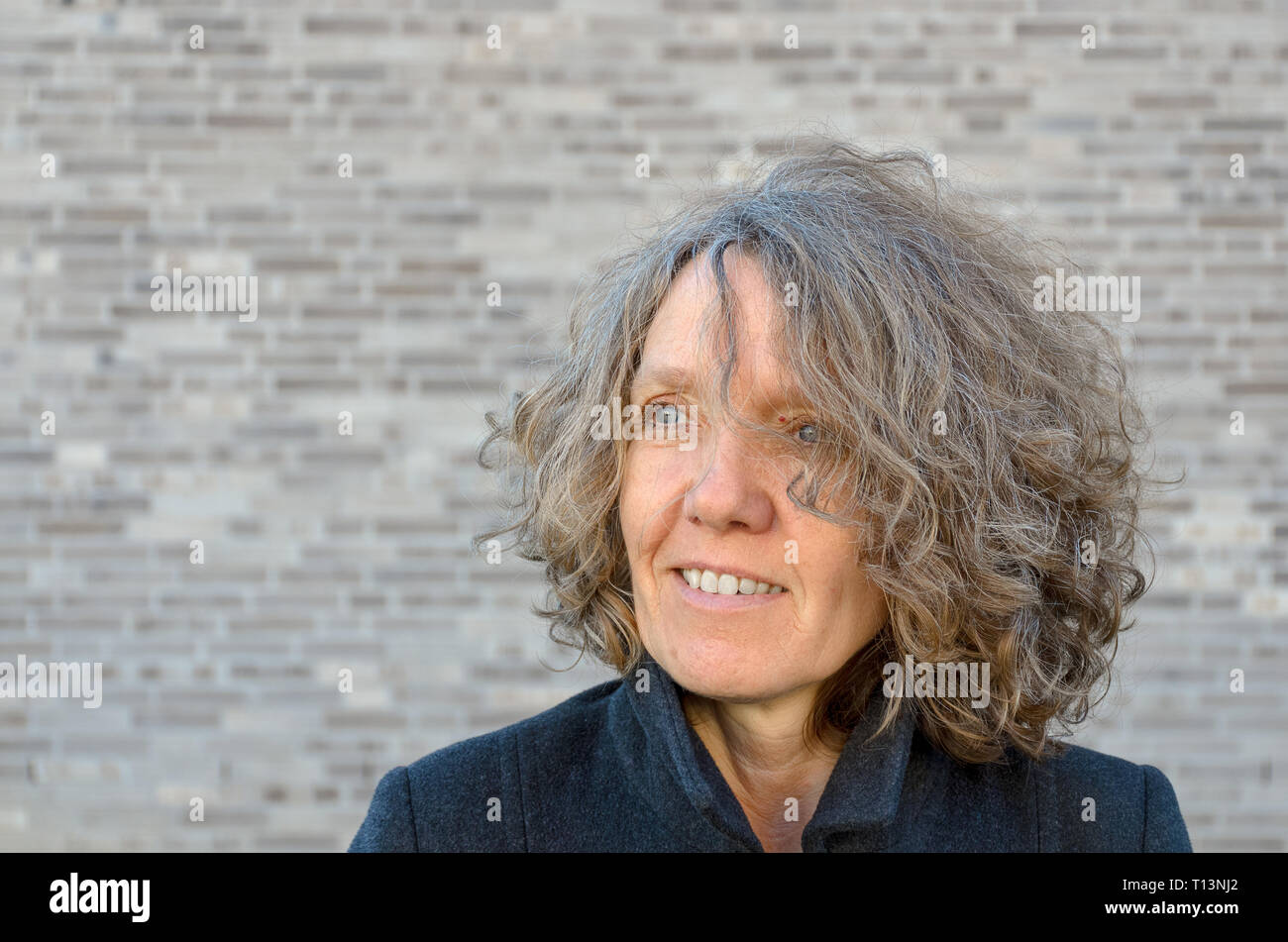 Mature smiling woman with curly tousled hair looking off to the side as ...
