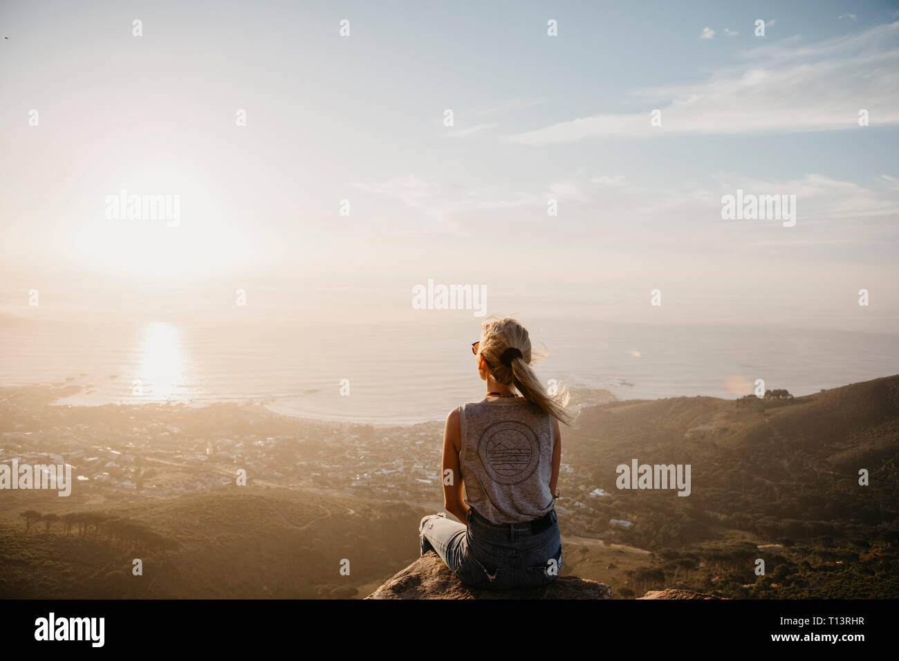 South Africa, Cape Town, Kloof Nek, woman sitting on rock at sunset ...