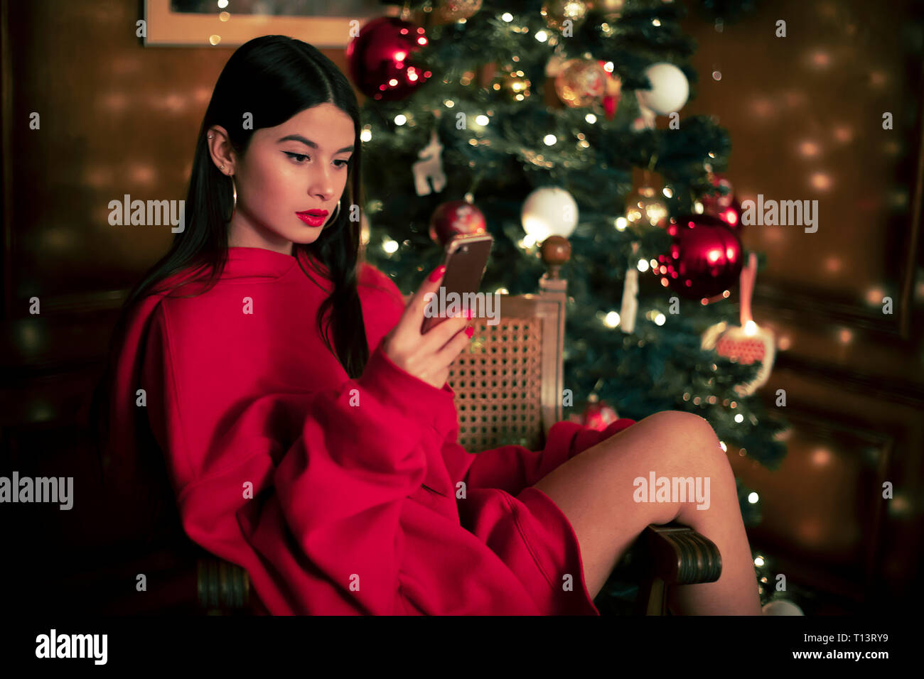 Portrait of teenage girl sitting in front of Christmas tree looking at ...