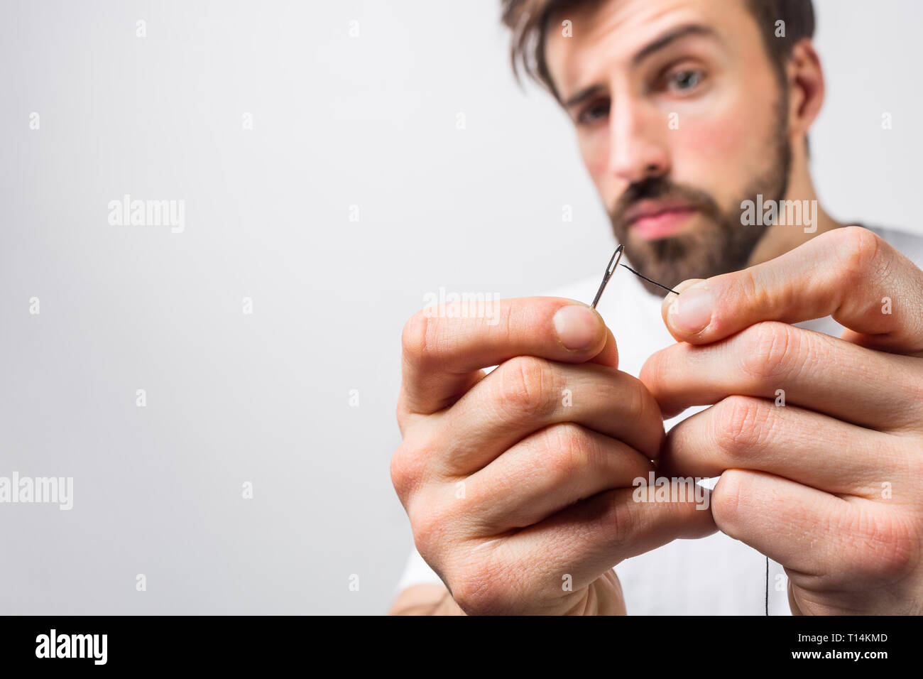 Serious and concentrated guy is trying to put a thread through an eye ...