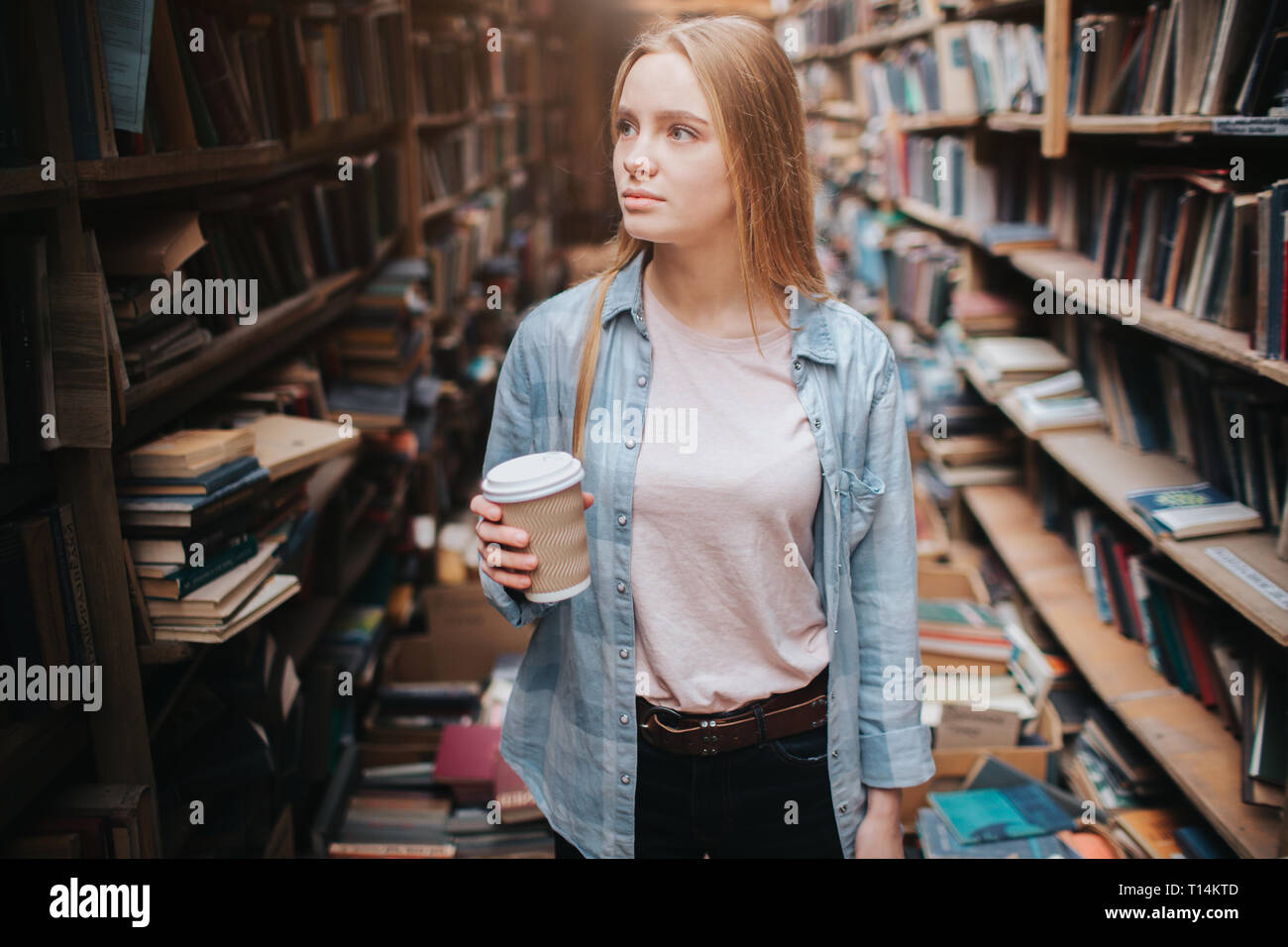 Attractive and nice girl is standing among big and long bookshelfs with ...