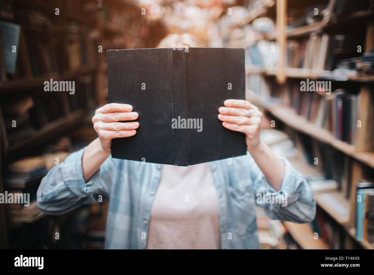Close up of a blonde girl holding a book and closing up her face with ...