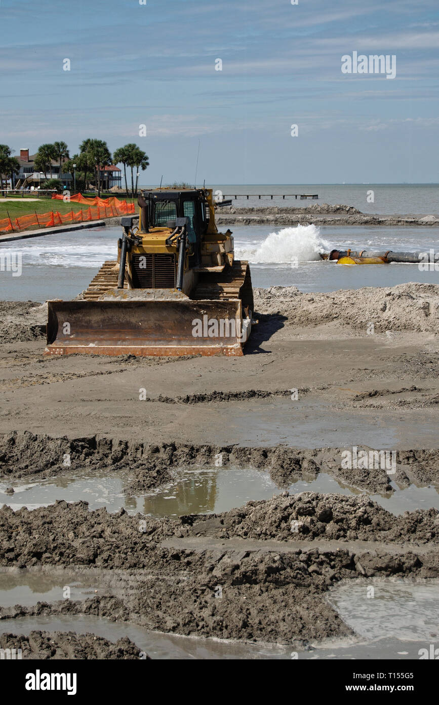 Bulldozer in the sand on the shore with water spraying out of pipe ...