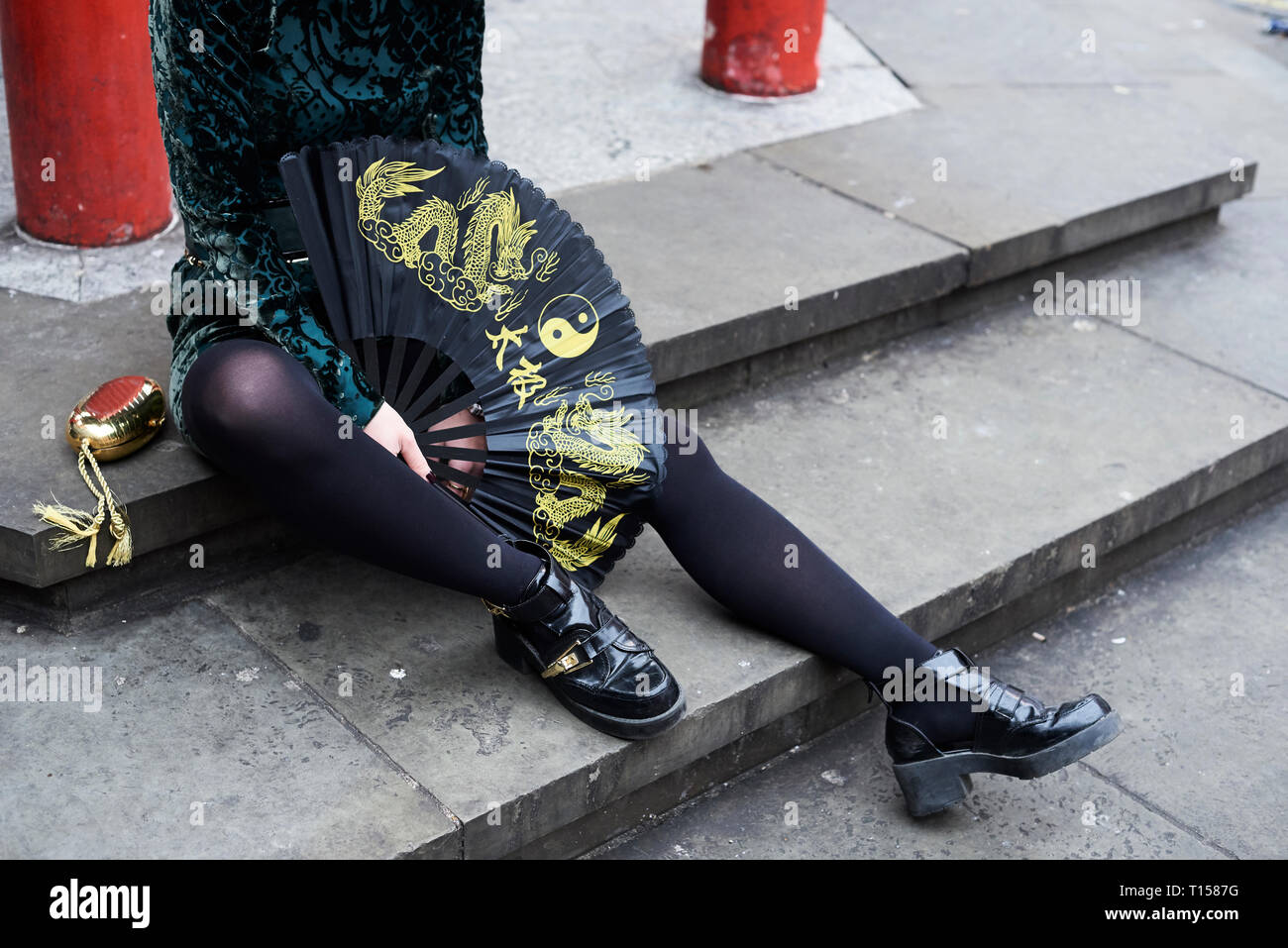 London, young woman with chinese fan in Chinatown, sitting on steps ...
