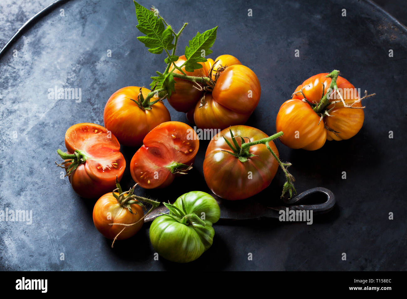 Whole and sliced beef tomatoes 'Chocolate Stripes' and knife on dark ...