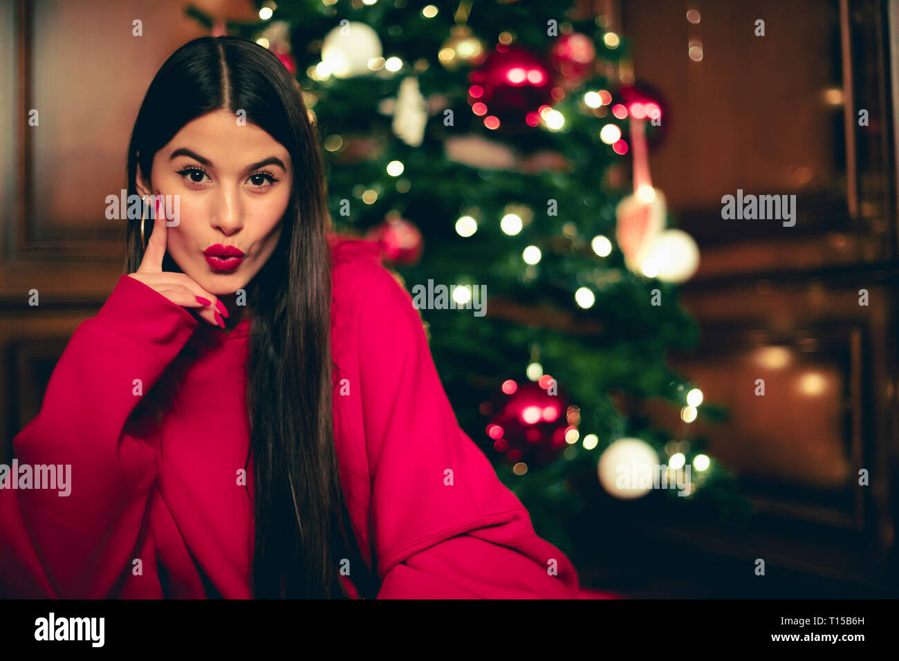 Portrait of teenage girl with Christmas tree in the background pouting ...