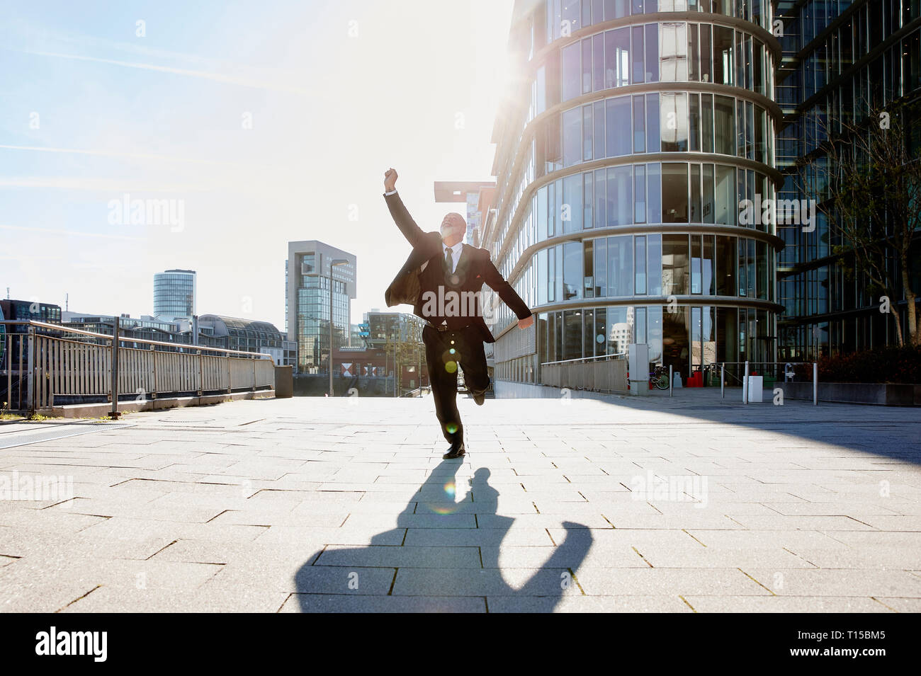 Businessman running in the city, raising hand, celebrating his success ...
