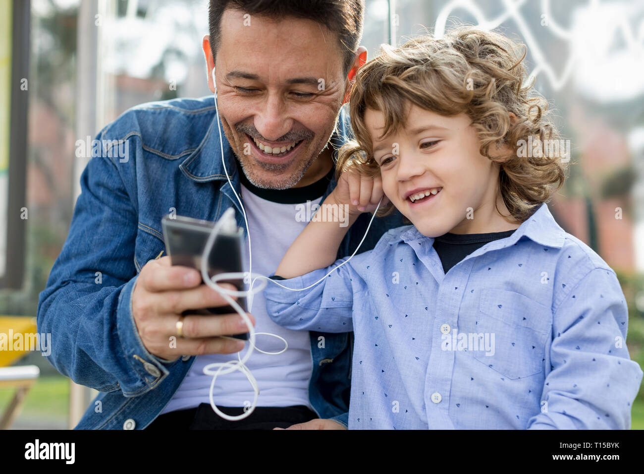Happy father and son sharing cell phone and earbuds Stock Photo - Alamy