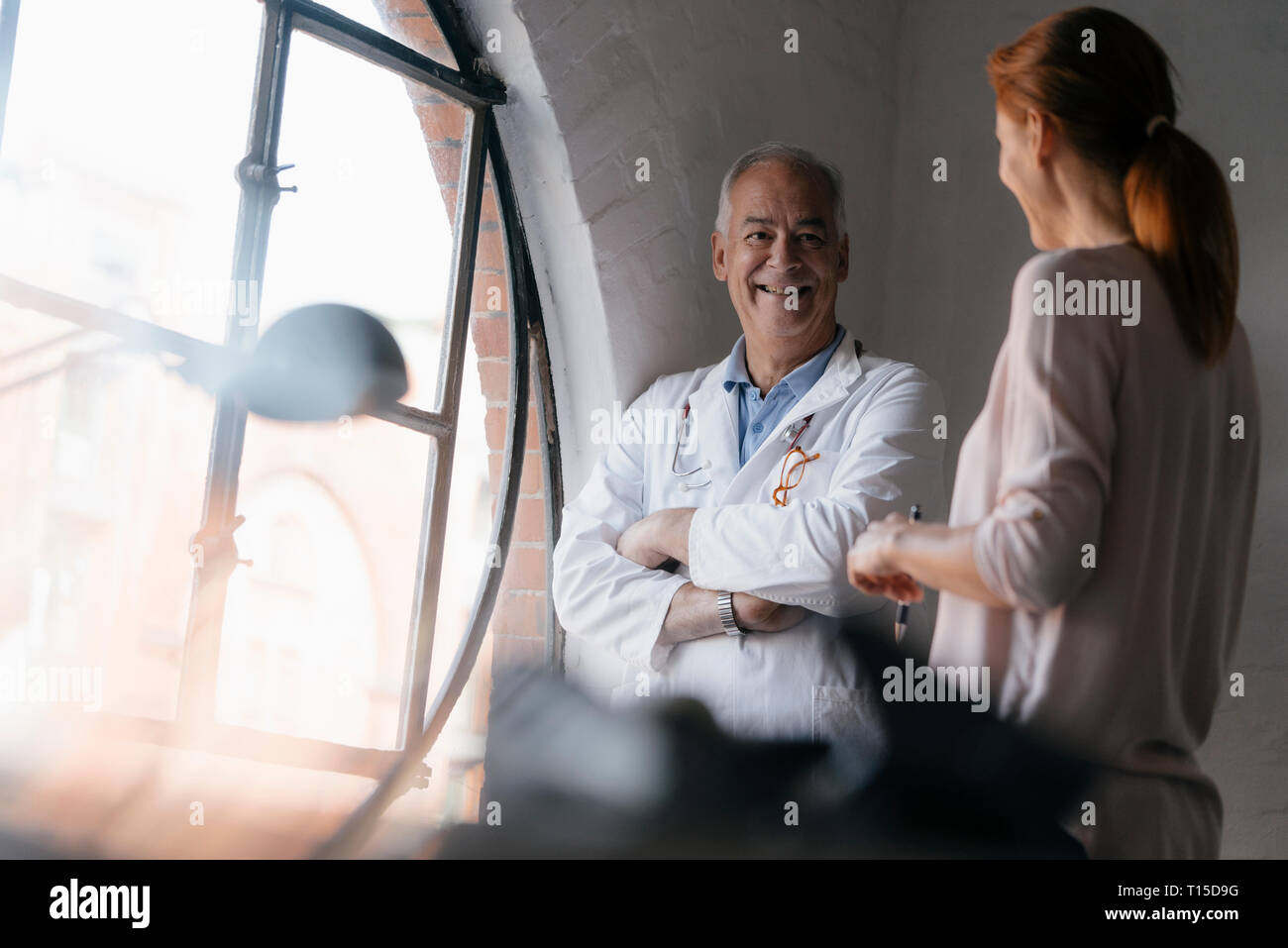 Smiling senior doctor talking to woman at the window in medical ...