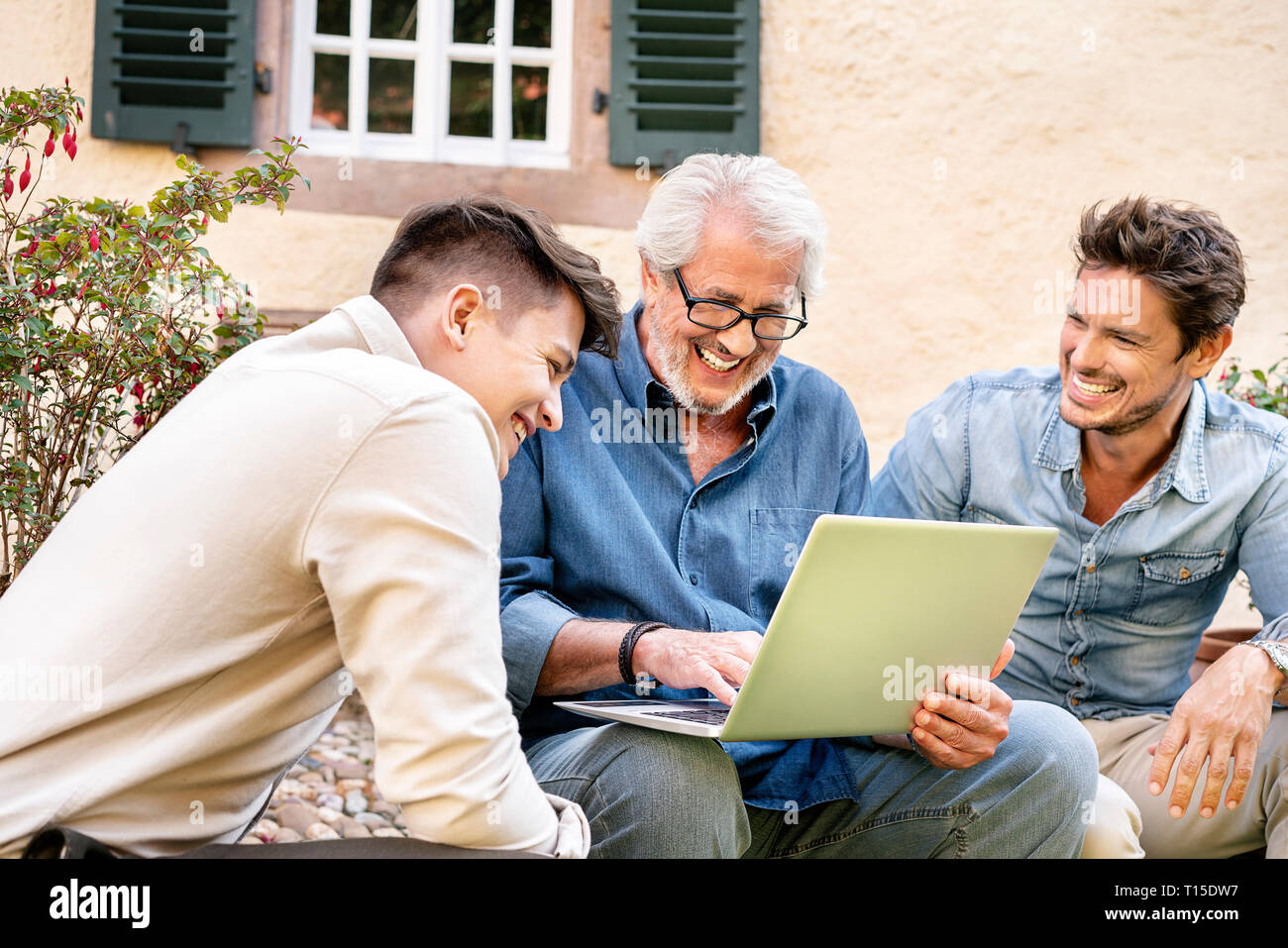 Three happy men of different age using laptop in garden Stock Photo - Alamy