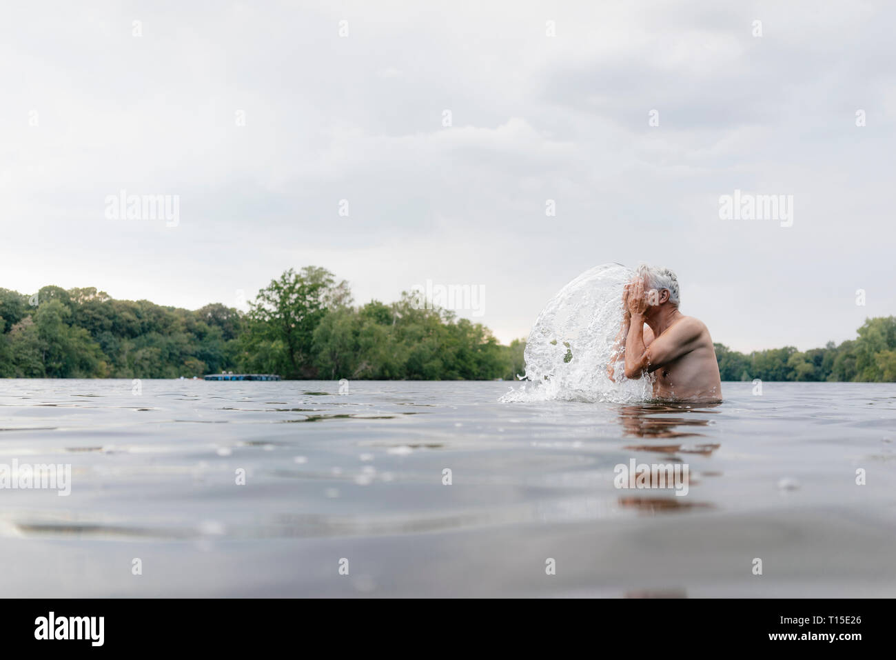 Senior man in a lake splashing water in his face Stock Photo - Alamy