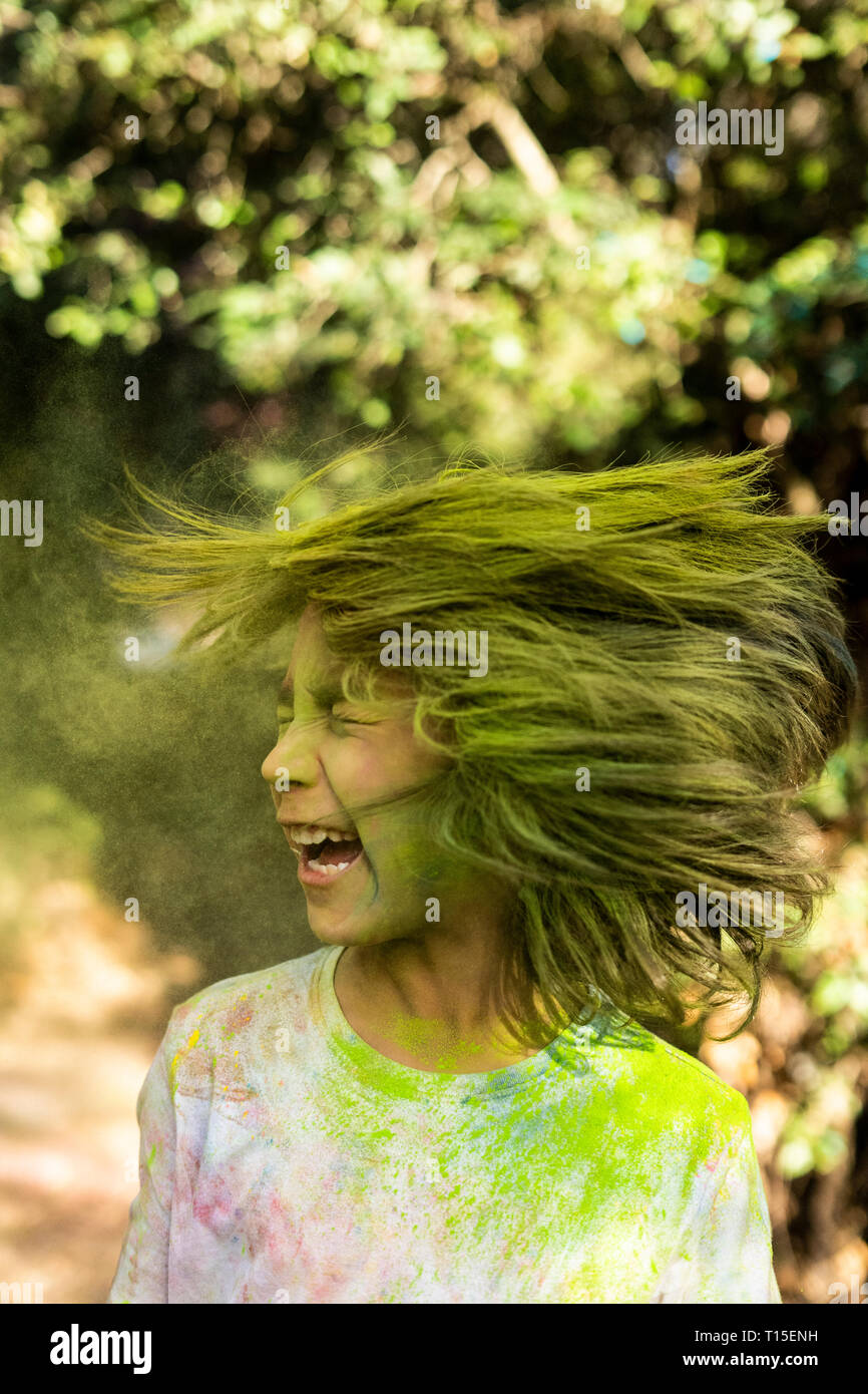 Boy shaking his head, full of colorful powder paint, celebrating Holi ...
