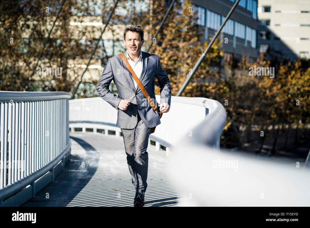 Businessman wearing full suit, running on a bridge Stock Photo - Alamy