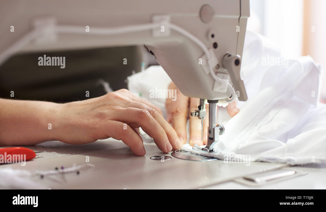 Female hands stitching white fabric on sewing machine at workplace with ...