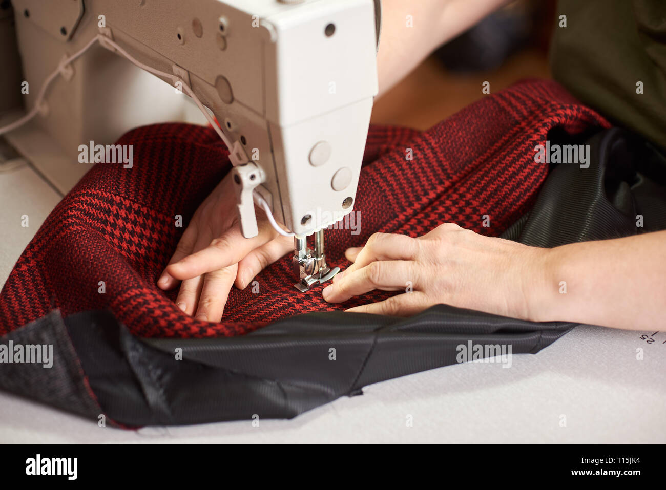 Female hands sewing plaid fabric on professional manufacturing machine ...