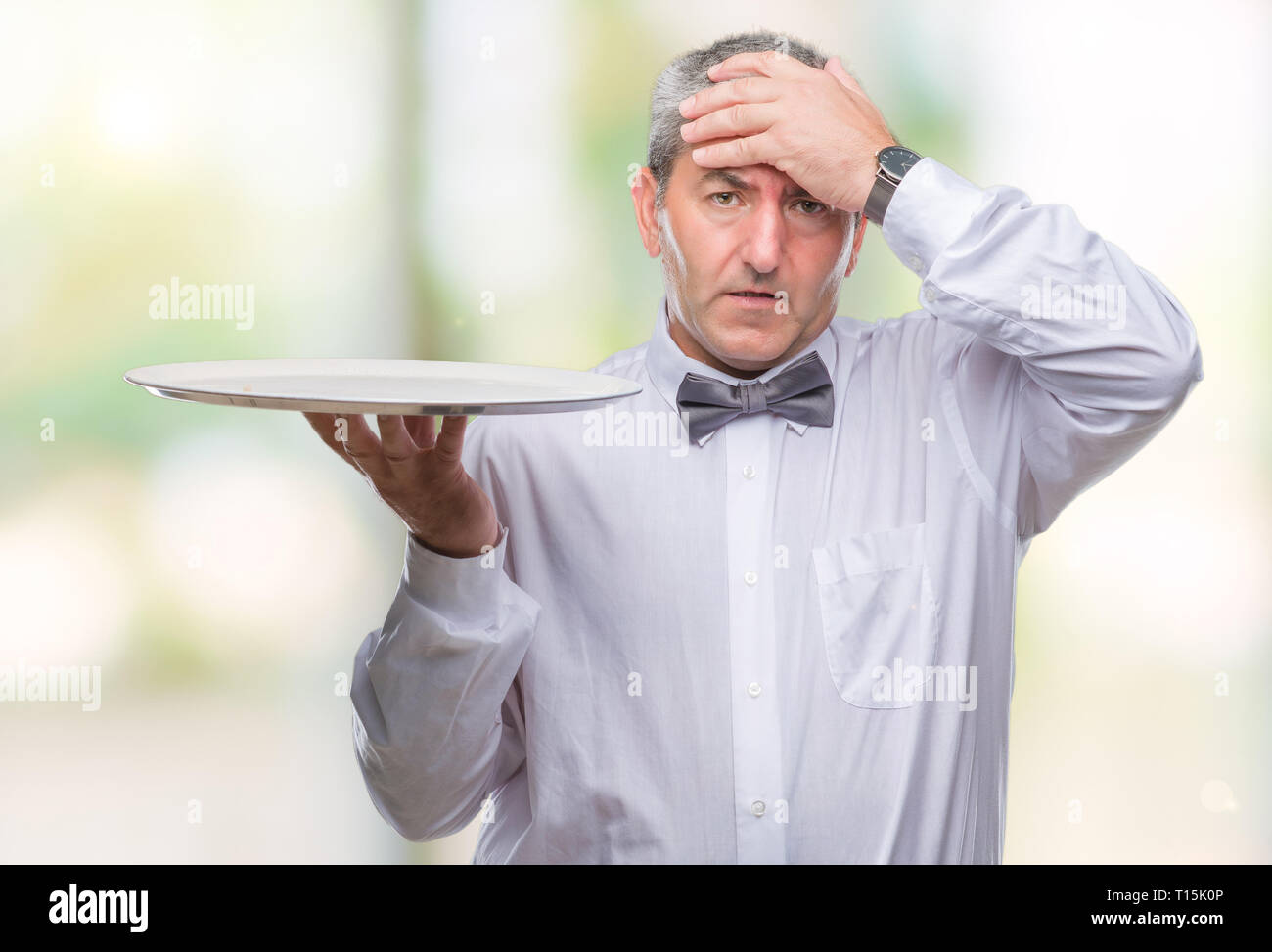 Handsome senior waiter man holding silver tray over isolated background ...