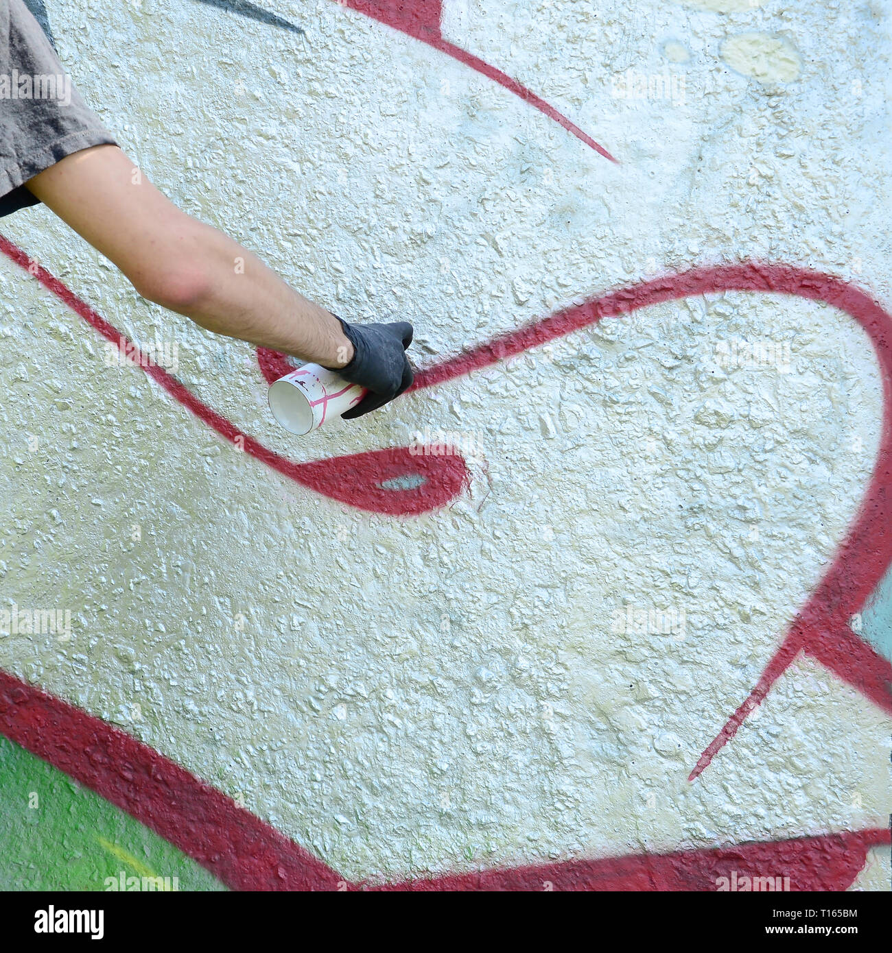 A hand in black gloves paints graffiti on a concrete wall. Illegal ...
