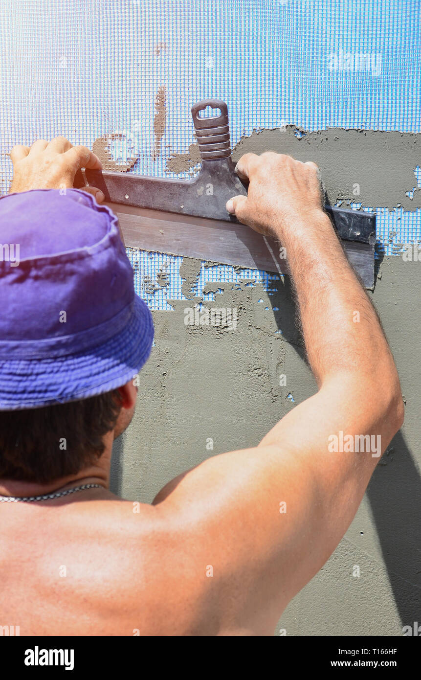 Fifty years old manual worker with wall plastering tools renovating ...