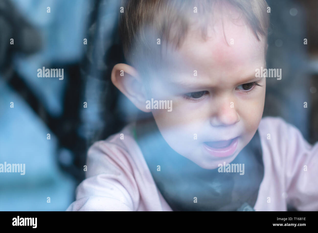 Beautiful cute baby boy looking in the window glass with reflection ...