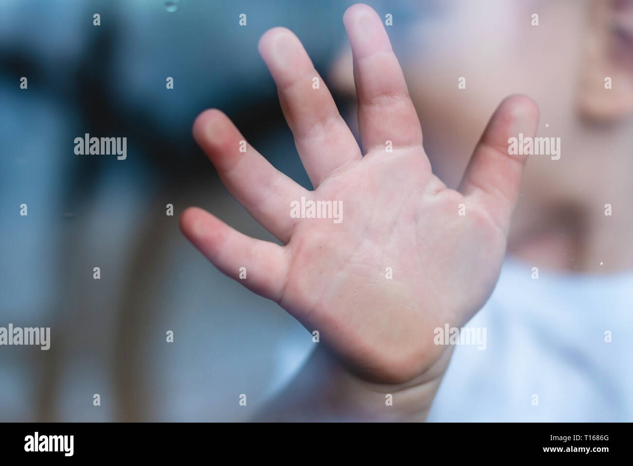 The child's small hand is pressed against the window glass with ...
