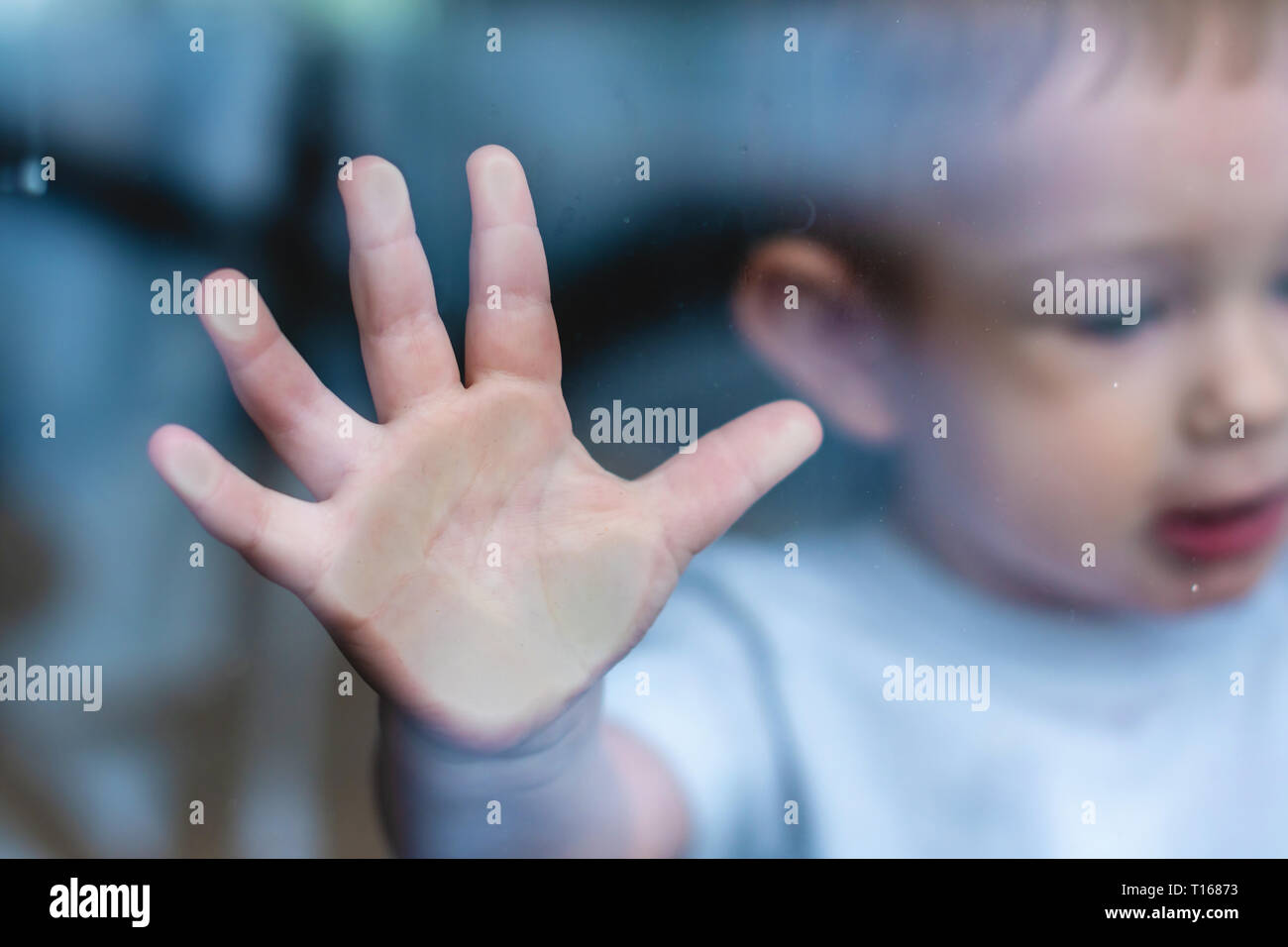 The child's small hand is pressed against the window glass with ...