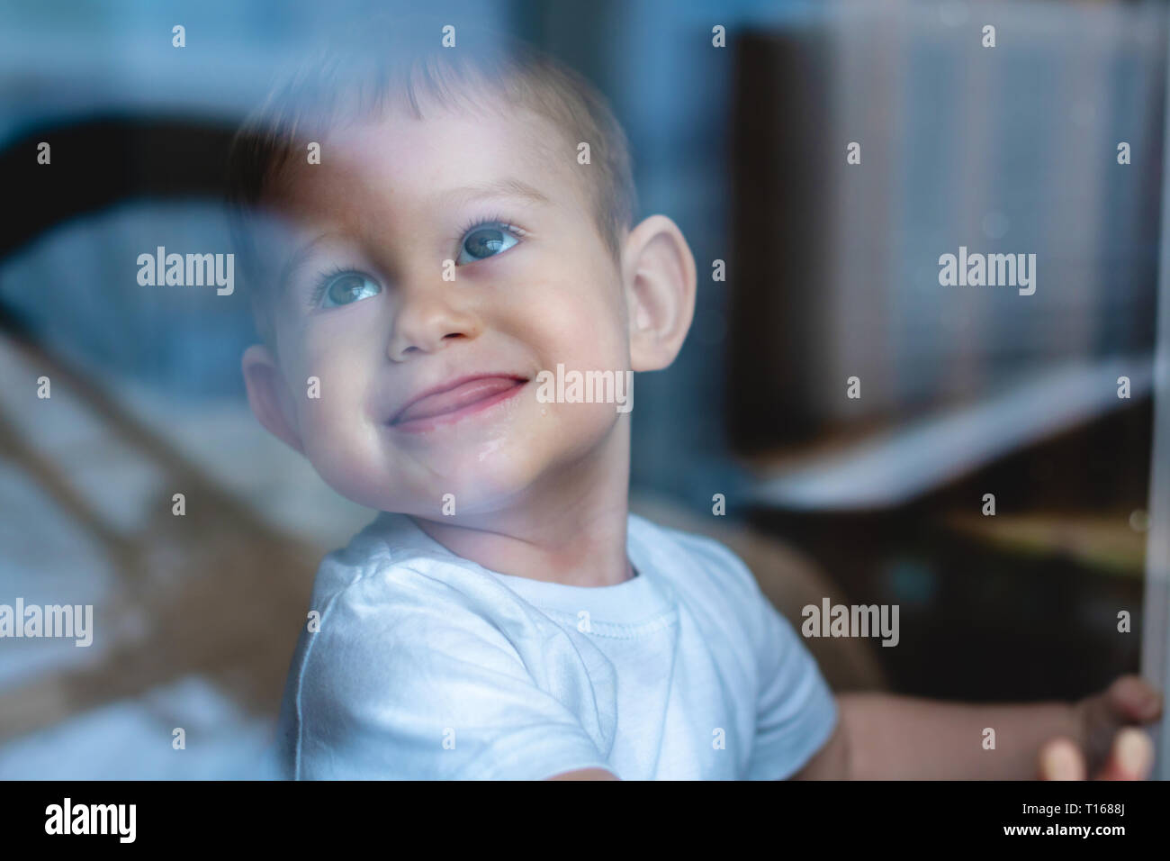 Beautiful cute baby boy looking in the window glass with reflection ...