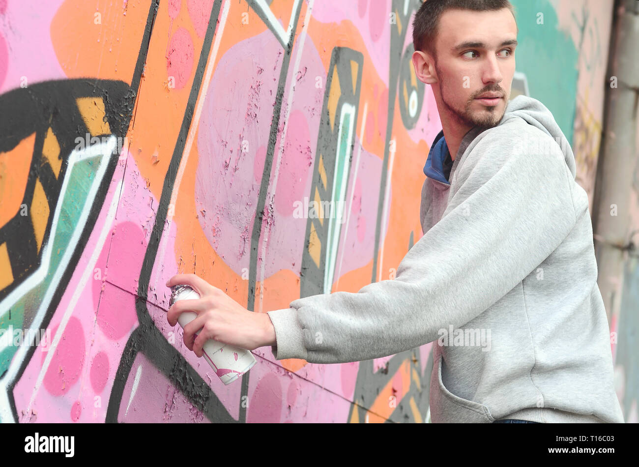 A young graffiti artist looks around while drawing. Vandal tries to be ...