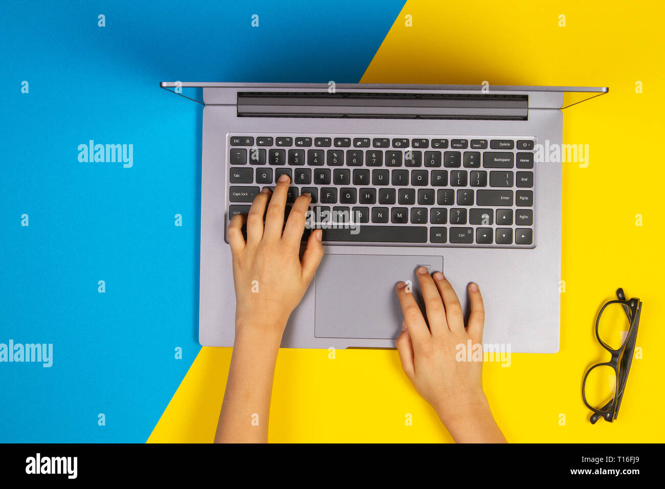 Kid hands typing on laptop computer keyboard on multicolored background ...