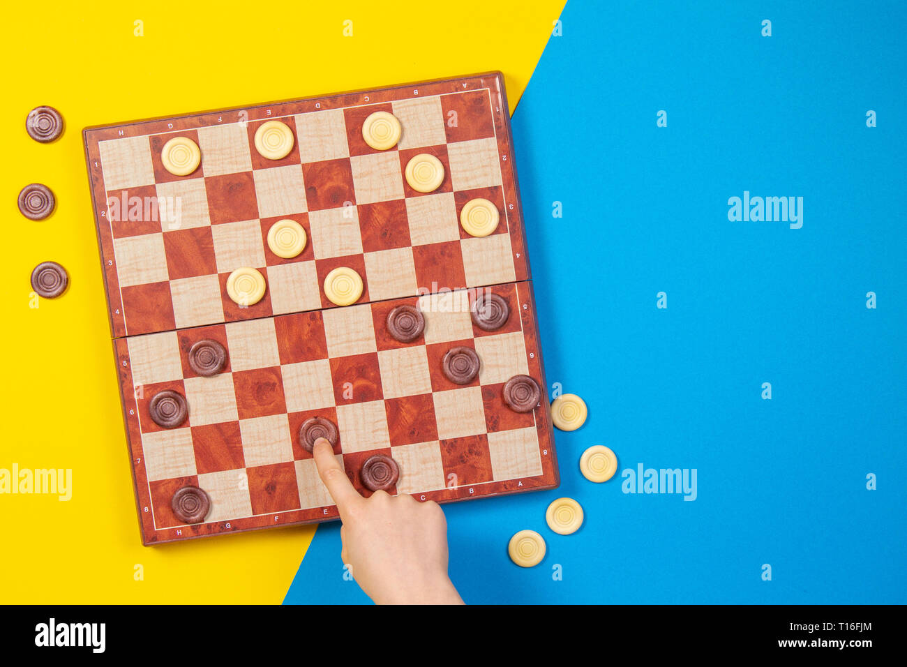 Child hands playing checkers on checker board game over yellow and blue ...