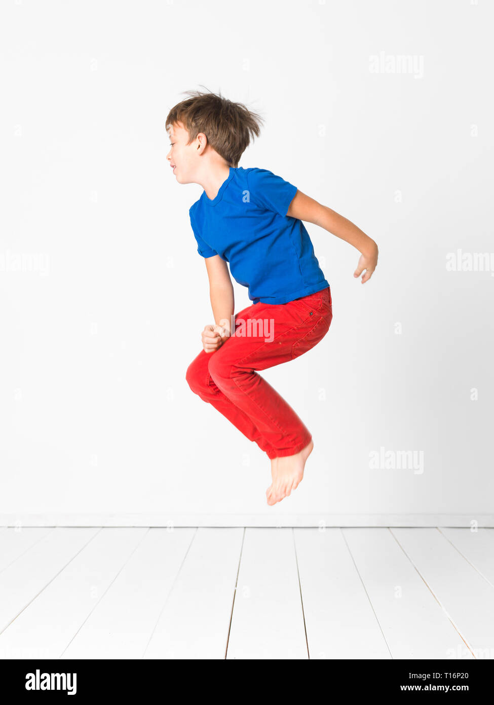 cool, cute boy with blue shirt and red trousers is jumping high in the ...