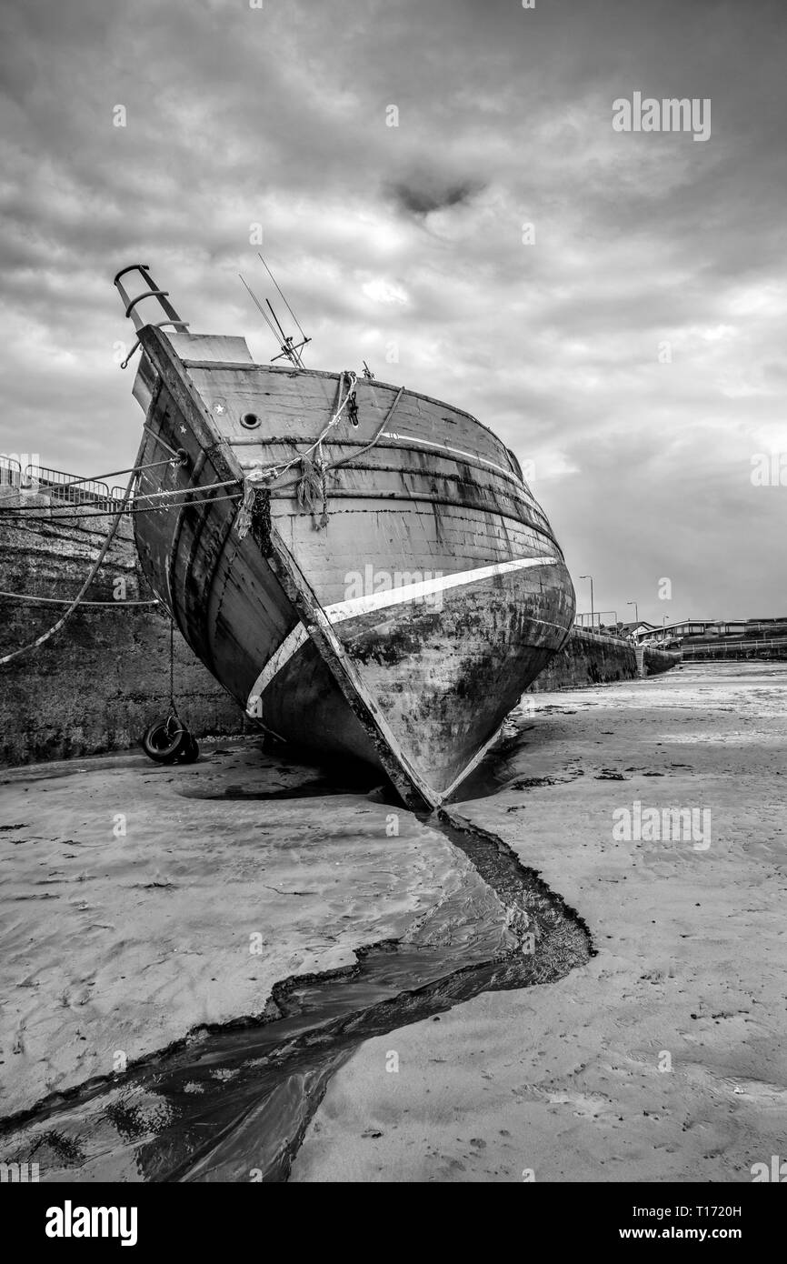 This is a black and white picture of an old fishing boat tide up to a ...