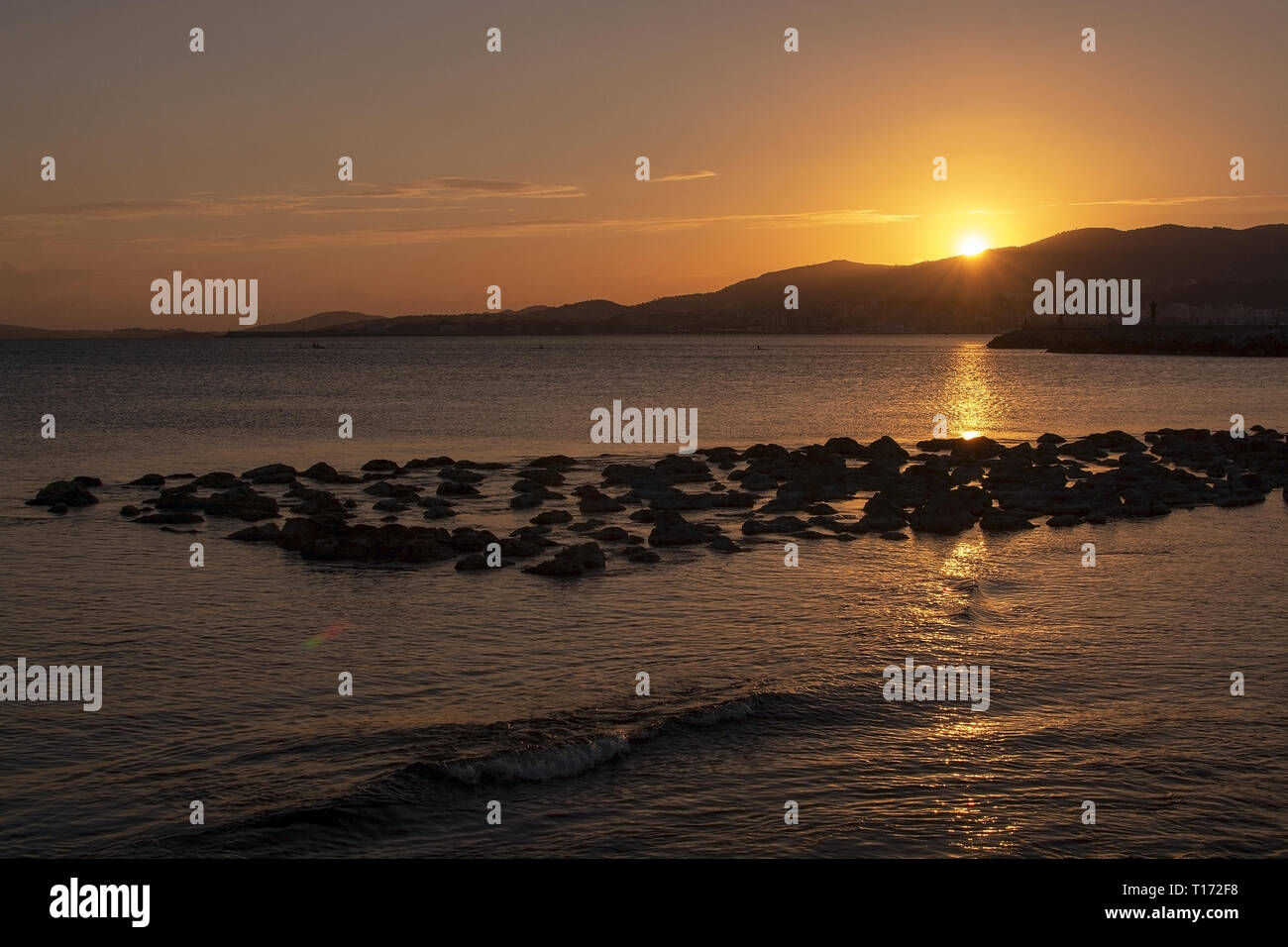 Beautiful golden sunset over mountains and ocean with string of rocks ...