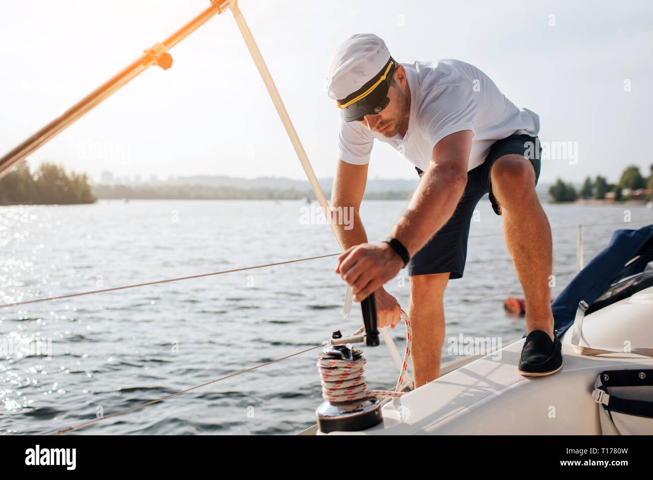 Picture of sailor stands on yacht and winds rope around. He is calm and ...