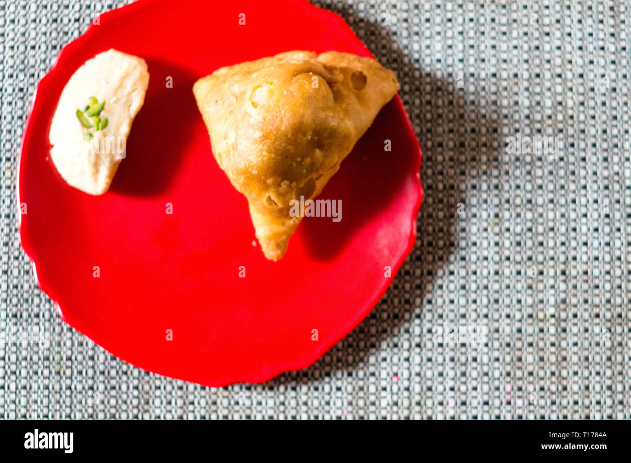 Samosa, peda barfi on red plate and woven mat, typical indian snack ...