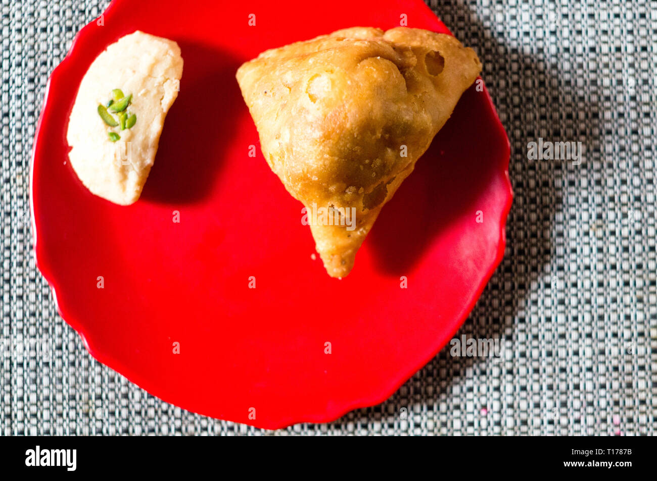 Samosa, peda barfi on red plate and woven mat, typical indian snack ...