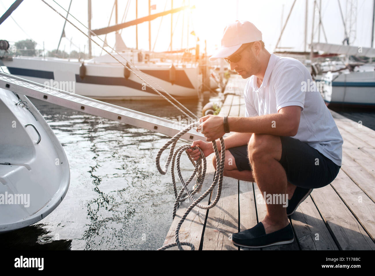 Picture of man in white cap and shirt sitting in squad position on pier ...