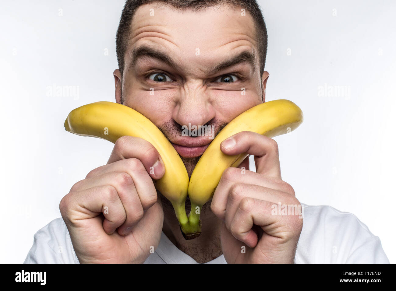 A freak man in white shirt is holding two bananas close to his face and ...